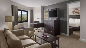 Quarto de hotel com sofá, escrivaninha, cômoda, televisão e cama.