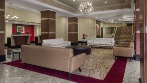 Um hall de entrada com balcão de recepção, sofás, um candelabro e uma escadaria.