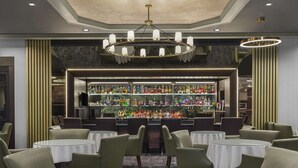 Uma área de bar com várias mesas e cadeiras, uma adega bem abastecida e um lustre moderno.