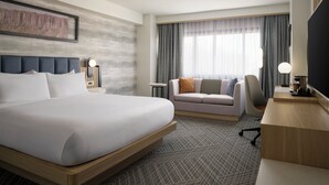 Quarto de hotel com cama, sofá, escrivaninha e televisão.