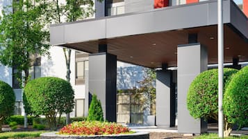 Um edifício moderno com entrada coberta, arbustos bem aparados e um jardim ajardinado.