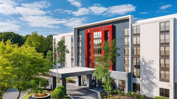 Um hotel moderno com fachada marcante em vermelho e branco, entrada coberta e jardins bem cuidados.