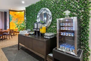 Quarto de hotel com estação de café, dispensador de suco e geladeira abastecida com iogurte.