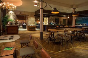 Restaurante com interior rústico, apresentando paredes de tijolo aparente, piso de madeira e diversos arranjos de assentos, incluindo mesas e cadeiras.