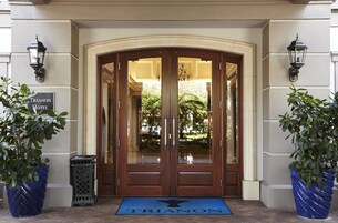 Entrada do Hotel Trionon, com portas duplas, plantas em vasos e um tapete azul com o nome do hotel.