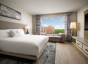 Quarto de hotel com uma cama grande, uma mesa pequena, um sofá, uma TV e uma janela com vista para um edifício.