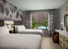 Quarto de hotel com duas camas, uma janela ampla com vista para uma piscina e edifícios, e design moderno.
