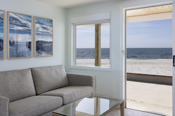 Quarto com sofá, mesa de centro de vidro e uma grande janela com vista para a praia.