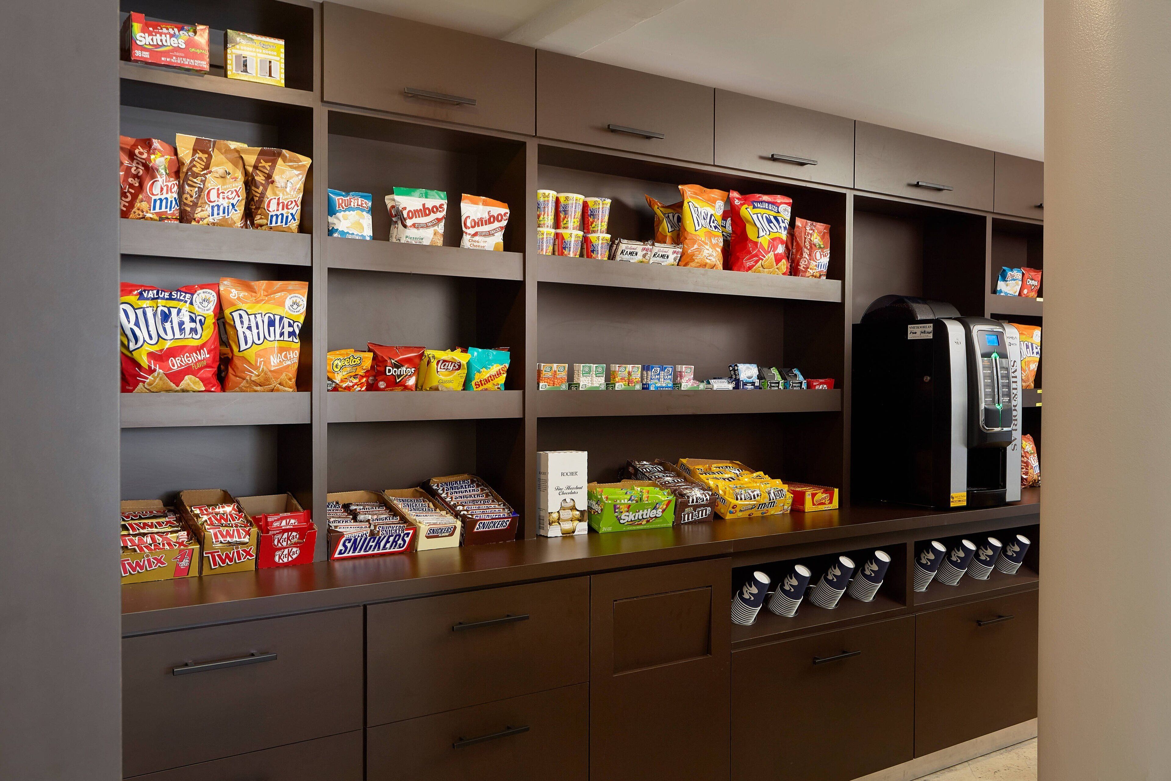 Exposição de lanches com diversas marcas, como Bugles, Twix e Skittles.