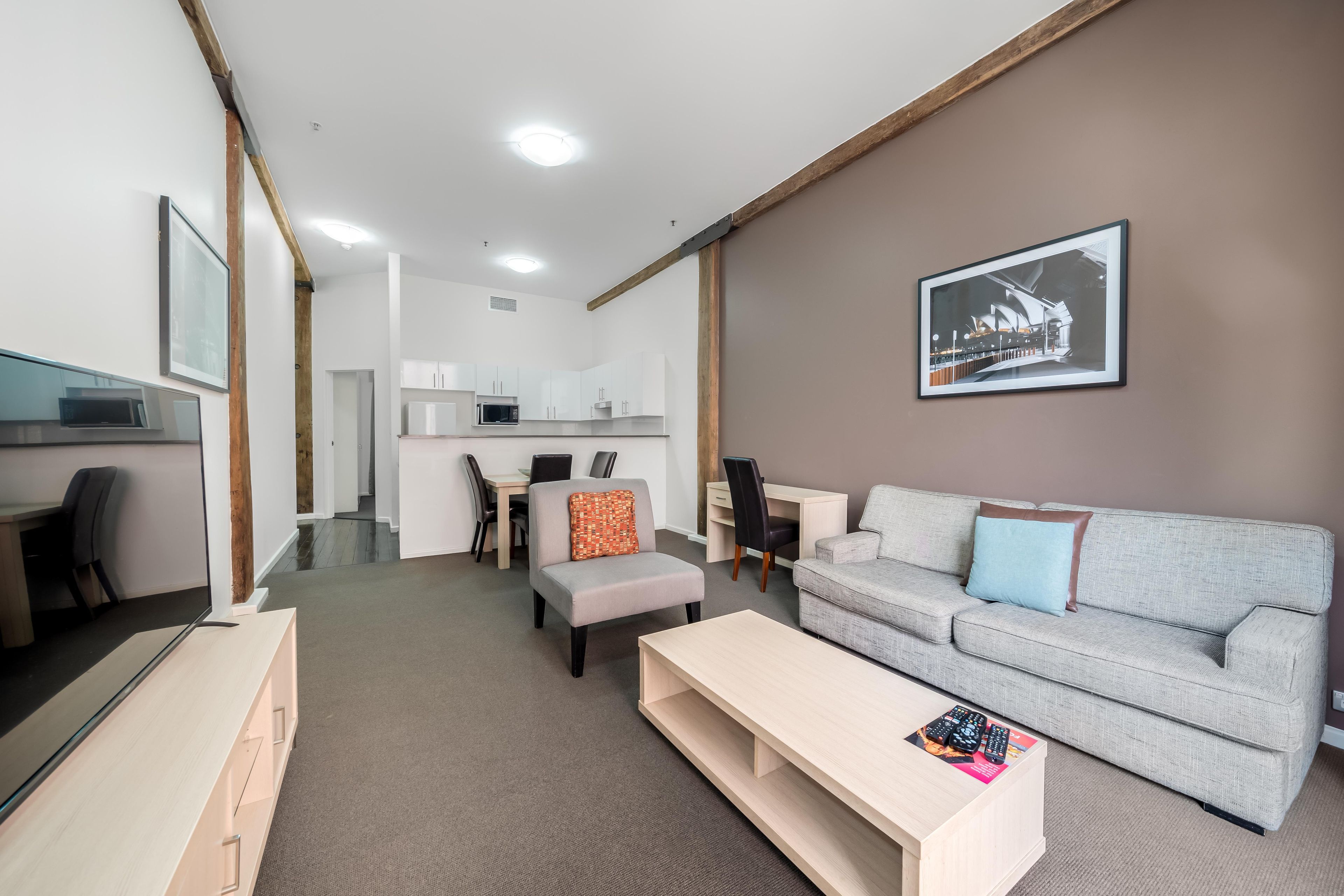 Uma sala de estar moderna com um sofá cinzento, uma mesa de centro e um espaço de refeições com uma mesa e cadeiras brancas.