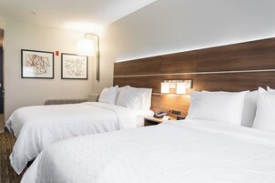 Quarto de hotel com duas camas, cabeceira de madeira, mesa de cabeceira com telefone e duas luminárias fixadas na parede.