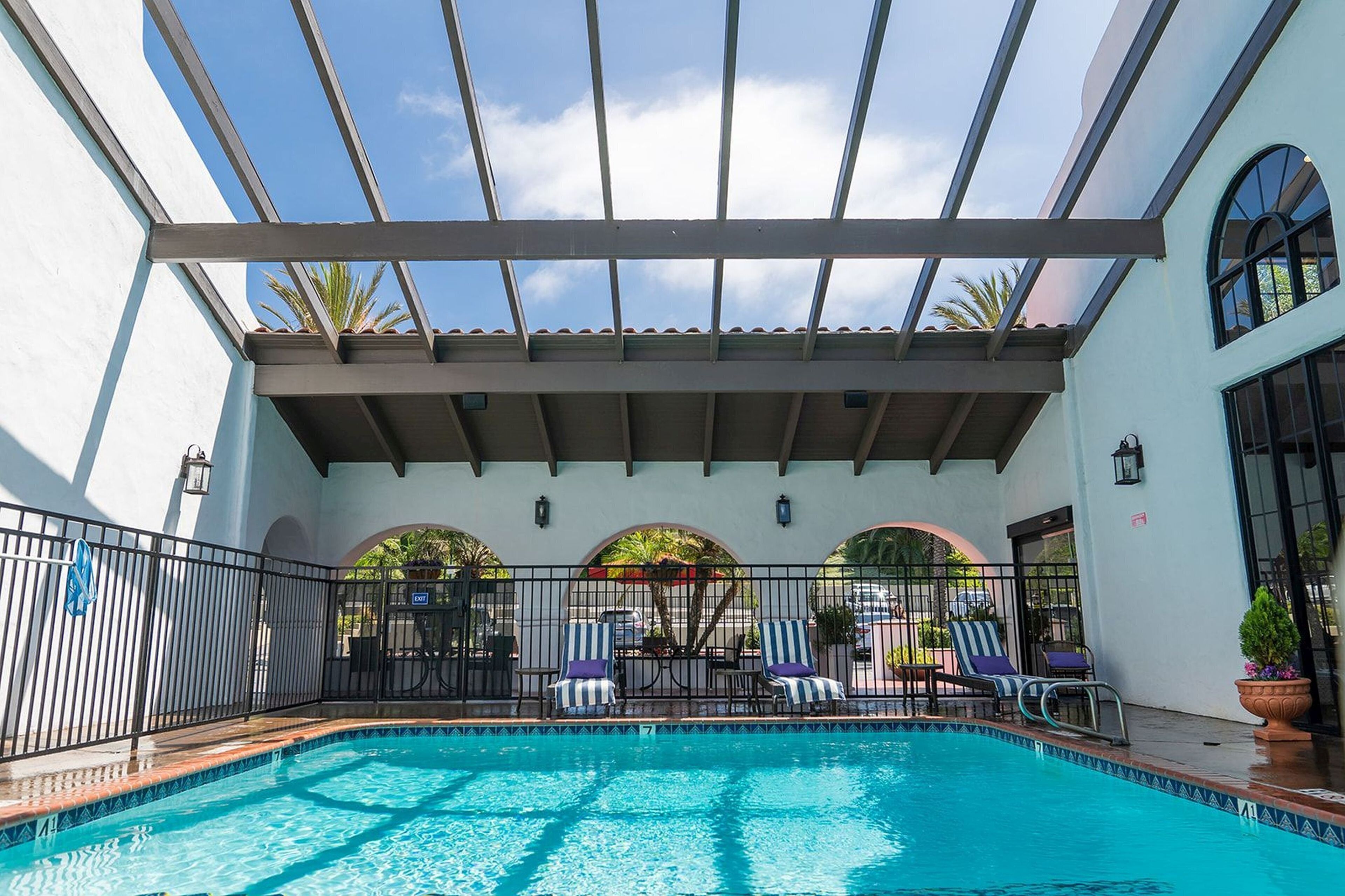 Piscina ao ar livre com área de estar coberta, espreguiçadeiras e céu azul.