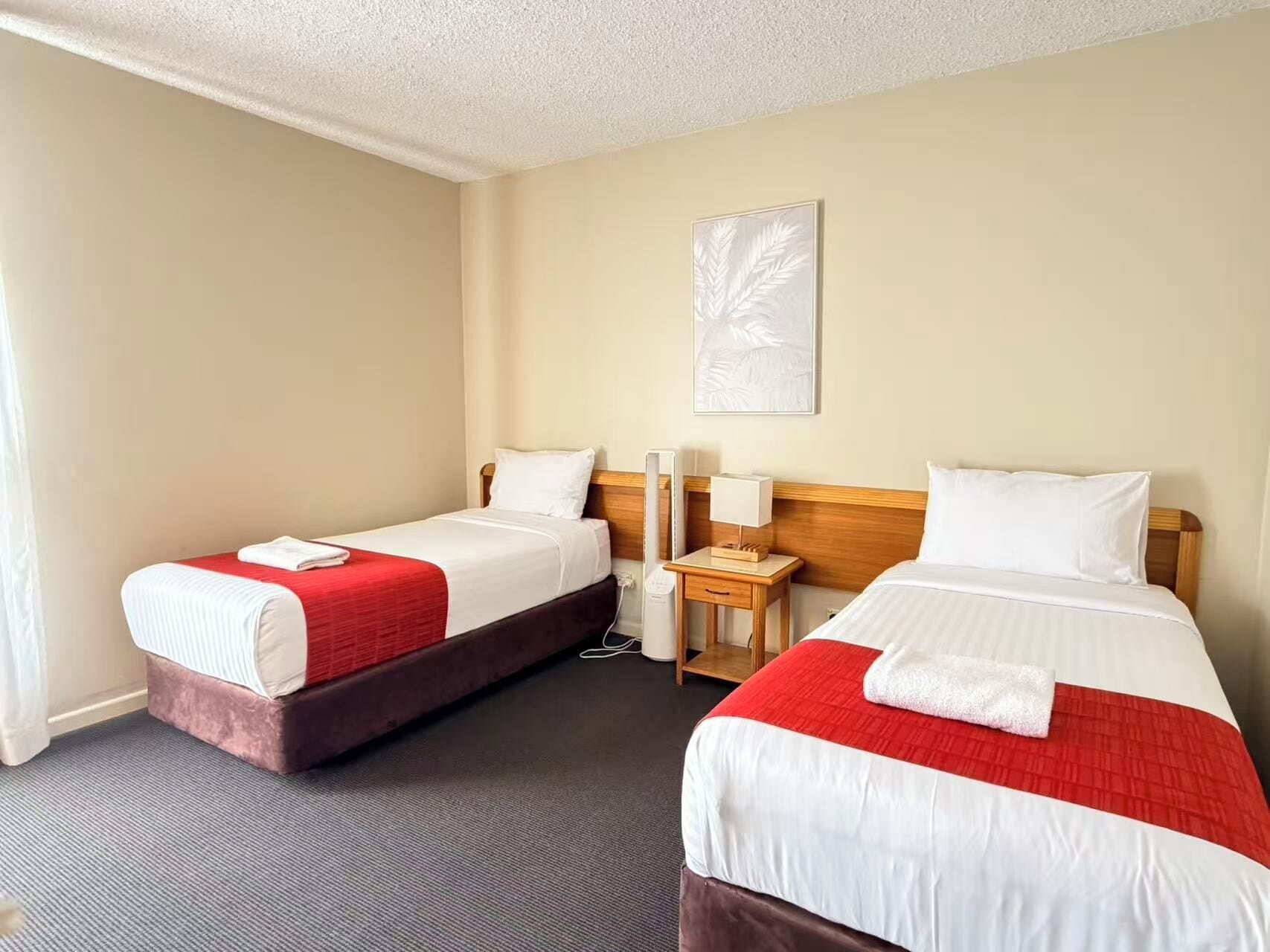 Quarto de hotel com duas camas, uma mesa de cabeceira, uma luminária e uma obra de arte na parede.