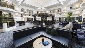Um hall amplo com área de estar central, vários níveis com grades e diversas opções de assento, incluindo sofás e cadeiras.