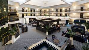 Um hall de hotel com vários níveis, com um bar central, áreas de estar e uma escadaria.