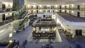 Um hall de hotel em vários níveis, com bar central, áreas de estar e uma escadaria.