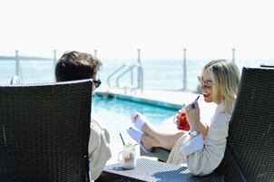 Duas pessoas sentadas à beira da piscina com uma bebida em frente.