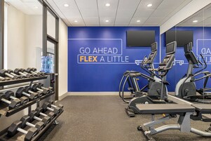 Uma academia com equipamentos de exercícios, halteres e frases motivacionais na parede.