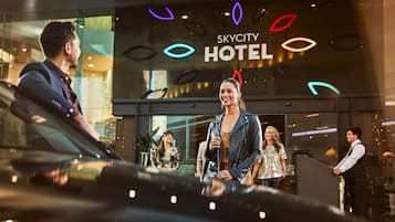 Entrada de hotel com design moderno, incluindo fachada de vidro e sinalização iluminada.
