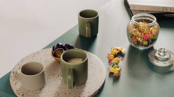 Duas canecas sobre um prato salpicado, um frasco com doces variados e um livro em cima de uma mesa.