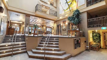 Um hall de hotel com vários níveis, uma escadaria central, uma receção e uma grande planta em vaso.
