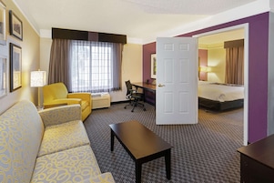 Quarto de hotel com sofá, escrivaninha, cadeira, cama e porta para outro cômodo.