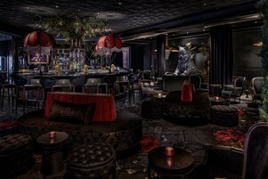 Uma área de bar com mesas redondas, assentos acolchoados e um grande guarda-sol vermelho.