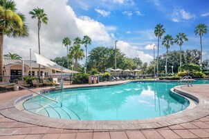 Uma área de piscina com espreguiçadeiras, palmeiras e um espaço coberto para relaxar.