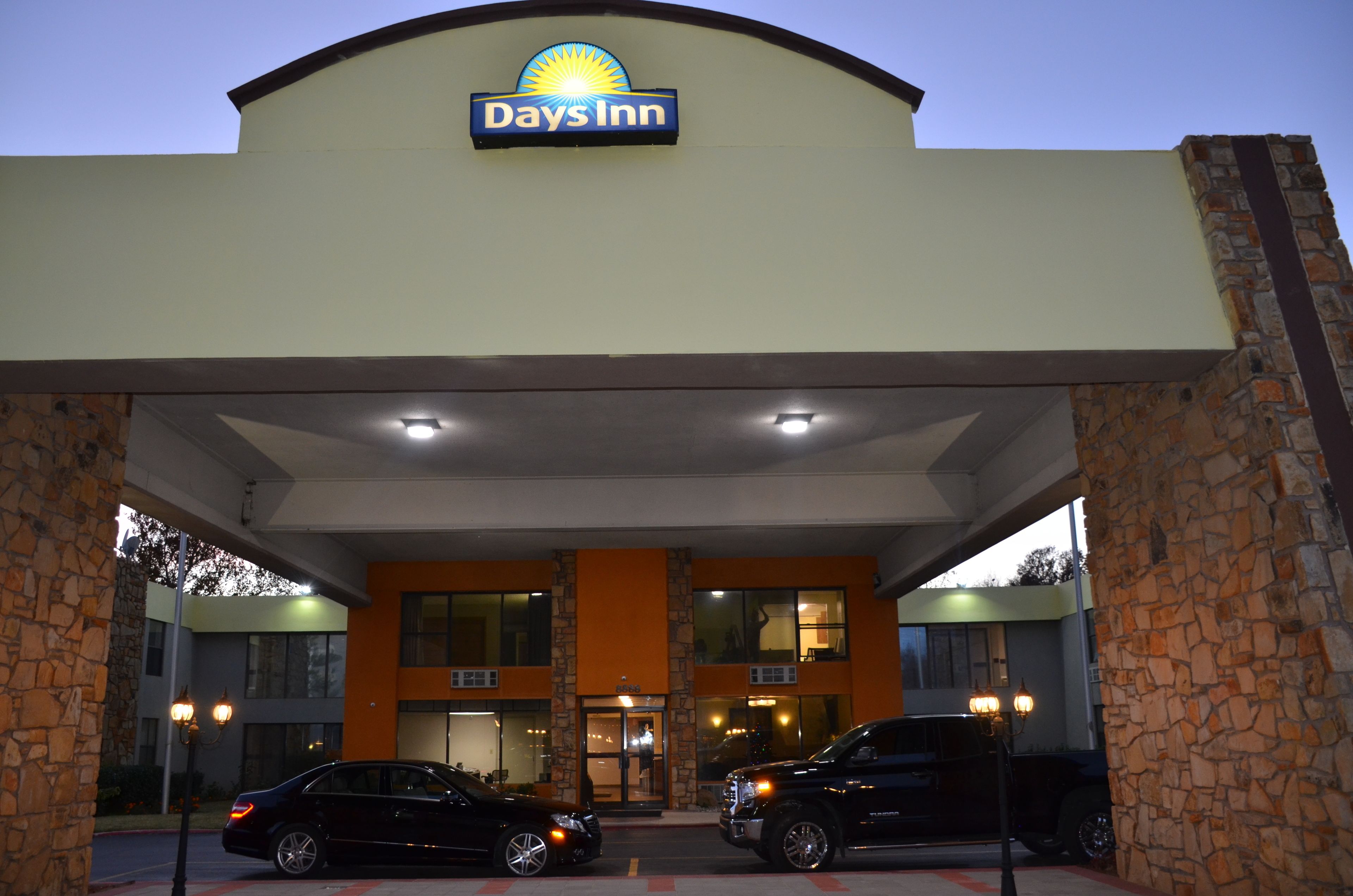 Um Days Inn com fachada de pedra, duas vagas de estacionamento e céu claro.