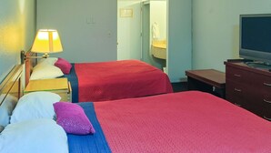 Quarto de hotel com duas camas, uma televisão, uma escrivaninha e um banheiro visível por uma porta aberta.