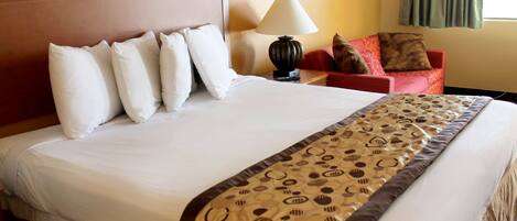Quarto de hotel com uma cama grande, uma luminária de cabeceira, uma poltrona vermelha e uma janela com cortinas.