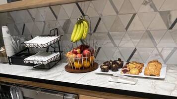 Uma bancada de cozinha com uma cesta de frutas, um suporte para bananas, uma bandeja de ovos e um prato de doces.