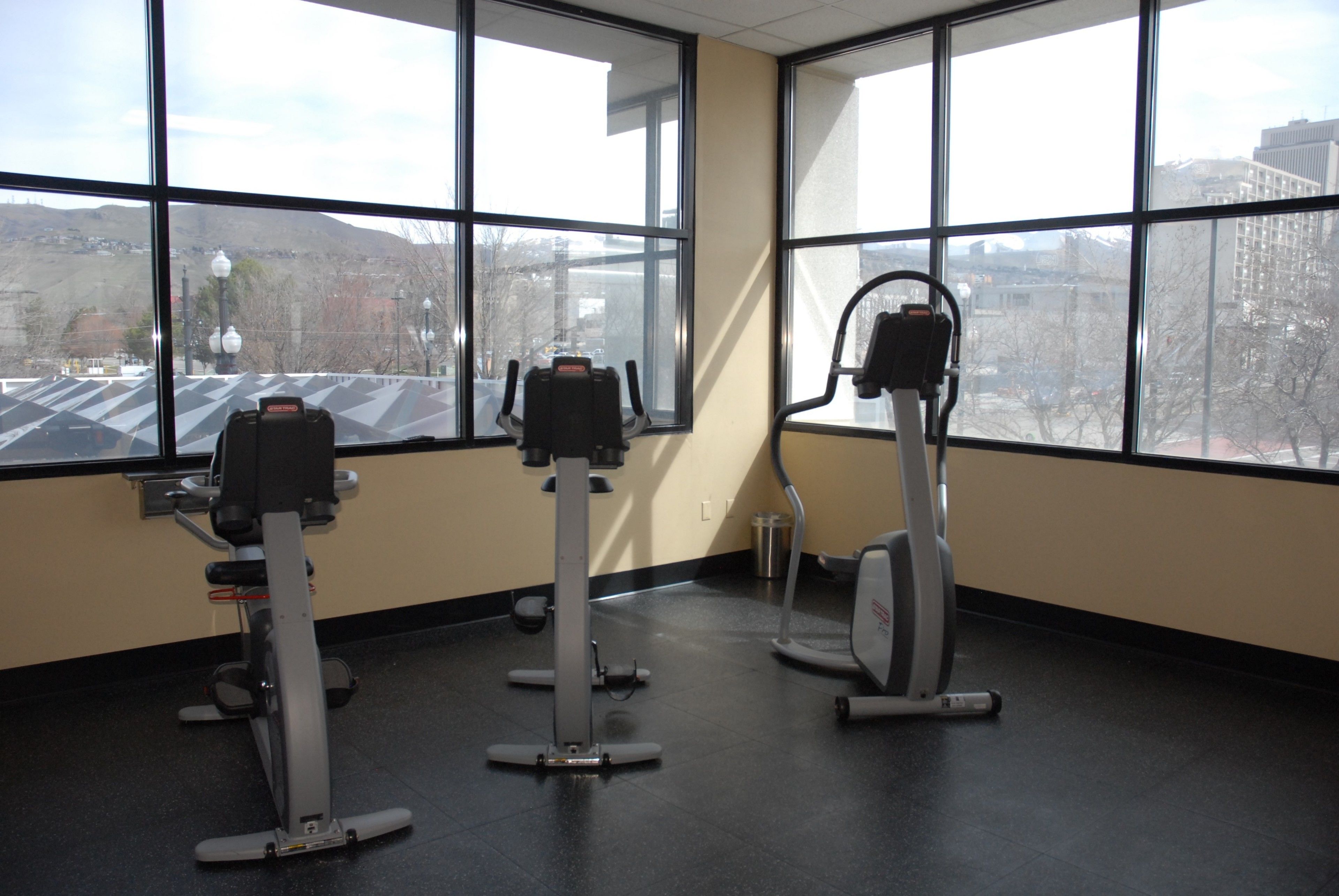 Academia com máquinas de cardio e amplas janelas com vista para a cidade.