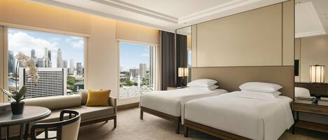 Quarto de hotel com duas camas, um sofá, uma escrivaninha e vista para o horizonte da cidade.
