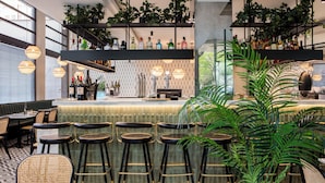 Uma área de bar moderna com prateleiras altas de garrafas, banquetas e um espaço de estar com mesas e cadeiras.