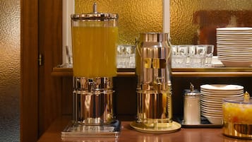 Disposição de buffet com uma grande tigela para ponche, um dispensador de café e pratos empilhados.