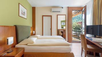 Quarto de hotel com duas camas, uma mesa, uma cadeira, uma televisão e varanda com vista para áreas verdes.