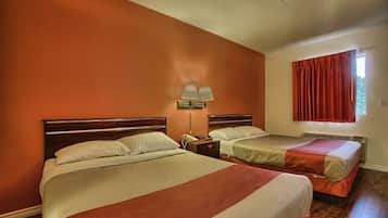 Quarto de hotel com duas camas, uma mesa de cabeceira com abajur e uma janela com cortinas vermelhas.