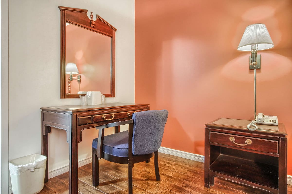 Quarto com escrivaninha de madeira, uma cadeira, um espelho, uma luminária e telefone em uma mesinha de cabeceira.