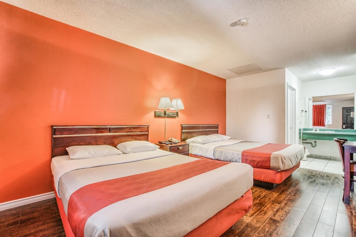 Quarto de hotel com duas camas, banheiro com pia verde e um espelho.