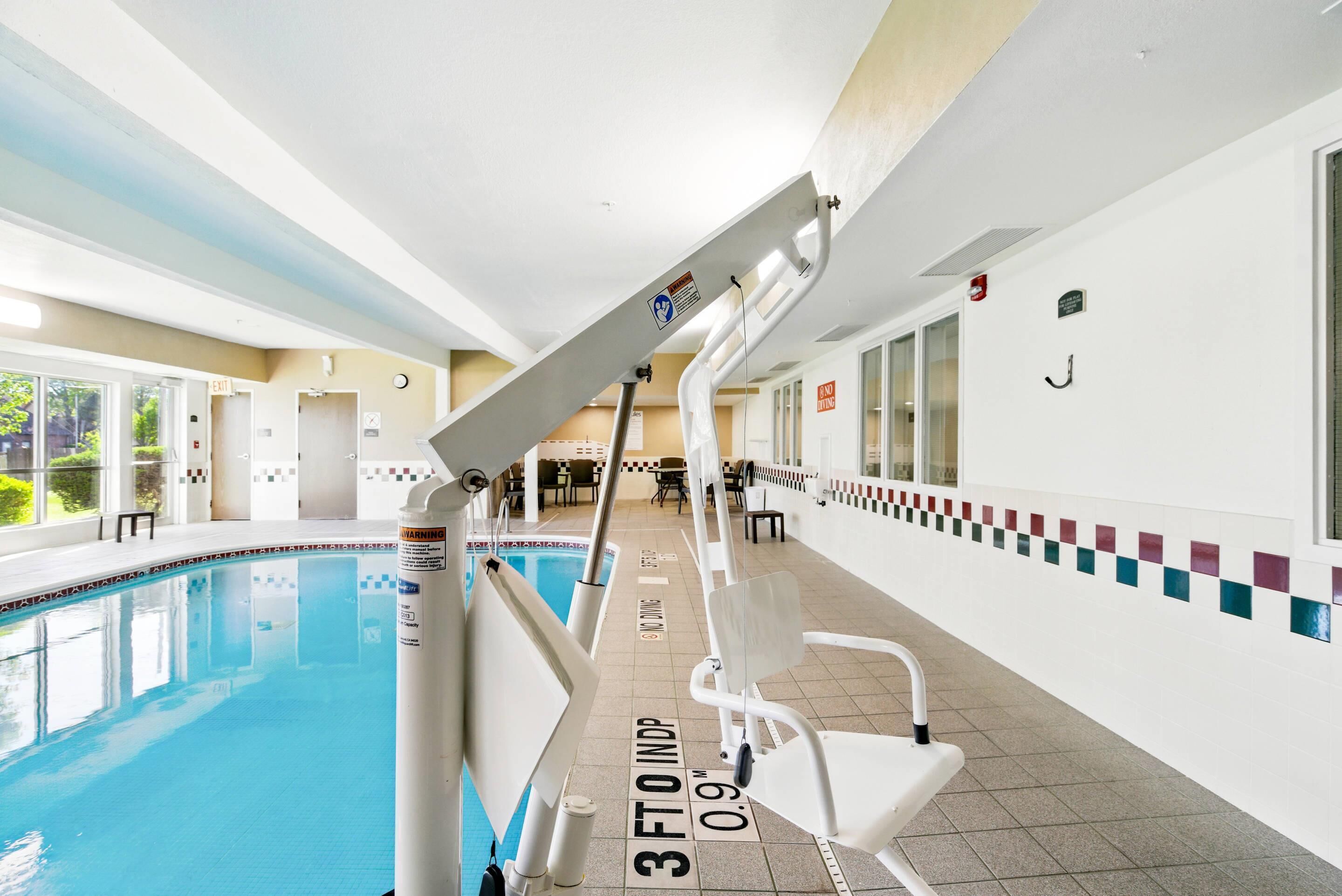 Piscina interior com prancha de mergulho, cadeira de salva-vidas e chão revestido com marcações de profundidade.