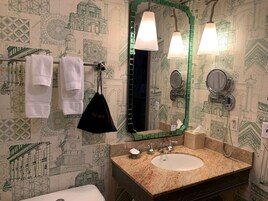 Um banheiro com pia, espelho, porta-toalhas e papel de parede estampado.