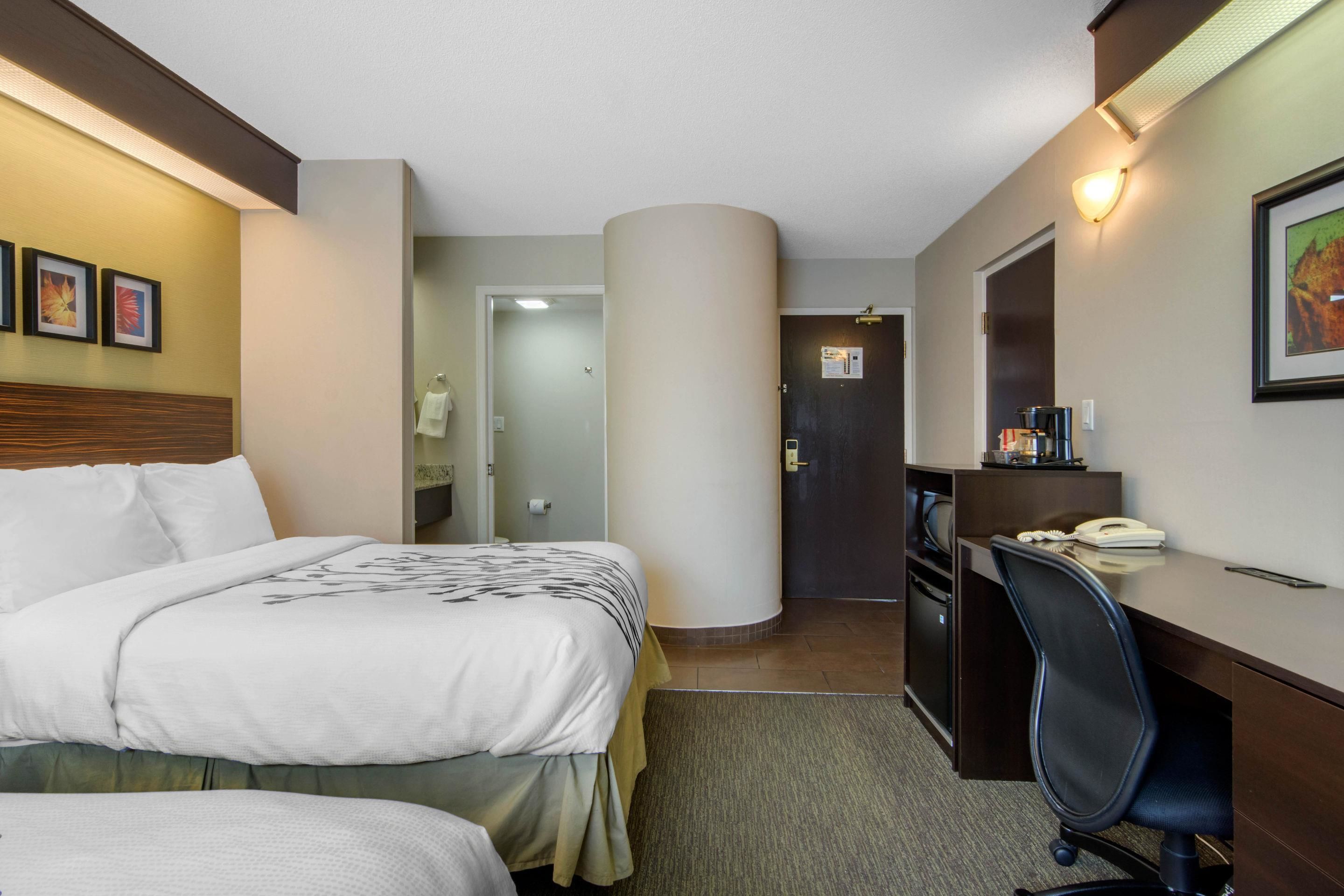Quarto de hotel com uma cama, uma escrivaninha e uma cadeira. Há uma porta que dá para o banheiro.