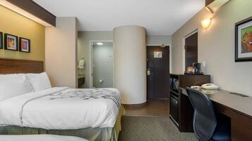 Quarto de hotel com uma cama, uma escrivaninha e uma cadeira. Há uma porta que dá para o banheiro.