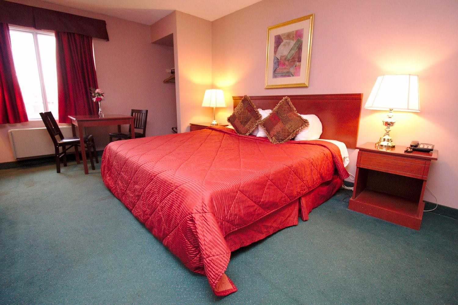 Quarto de hotel com uma cama grande, duas mesas de cabeceira com luminárias, uma escrivaninha com cadeira e uma janela com cortinas.