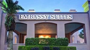Fachada do hotel Embassy Suites, com entrada destacada, um jardim bem cuidado e o nome do hotel exibido acima da entrada.