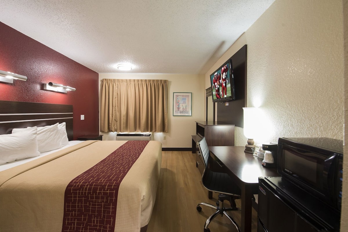 Quarto de hotel com cama, escrivaninha, cadeira, televisão e janela com cortinas.