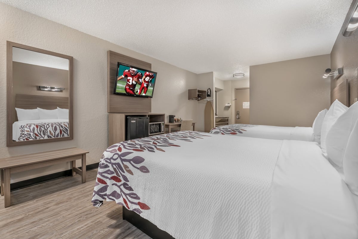 Quarto de hotel com duas camas, televisão, escrivaninha e espelho.