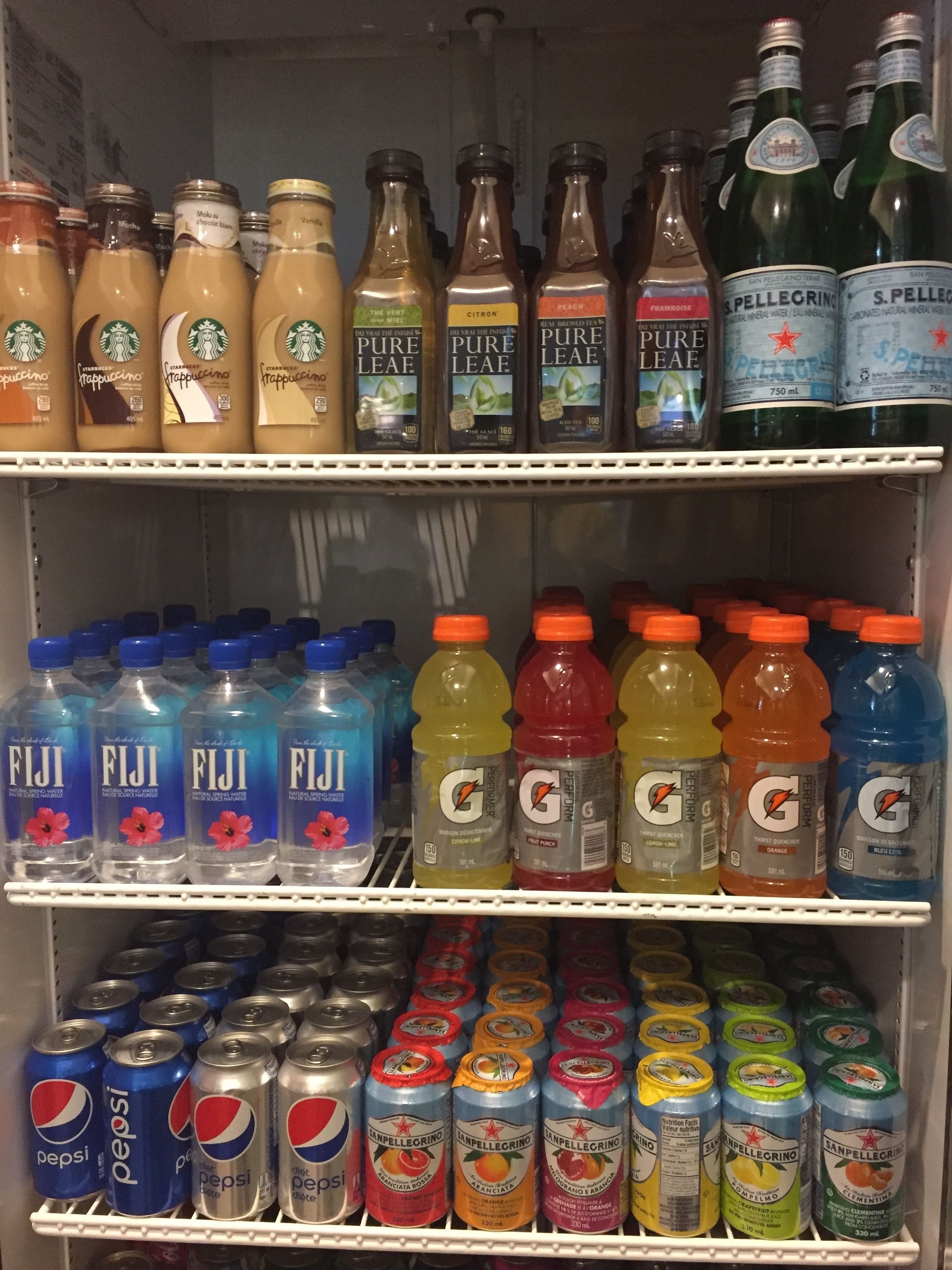 Geladeira de bebidas abastecida com diversas opções, incluindo água engarrafada, refrigerantes e bebidas energéticas.