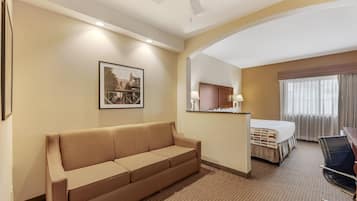 Quarto de hotel com sofá, cama, escrivaninha e ventoinha no teto.